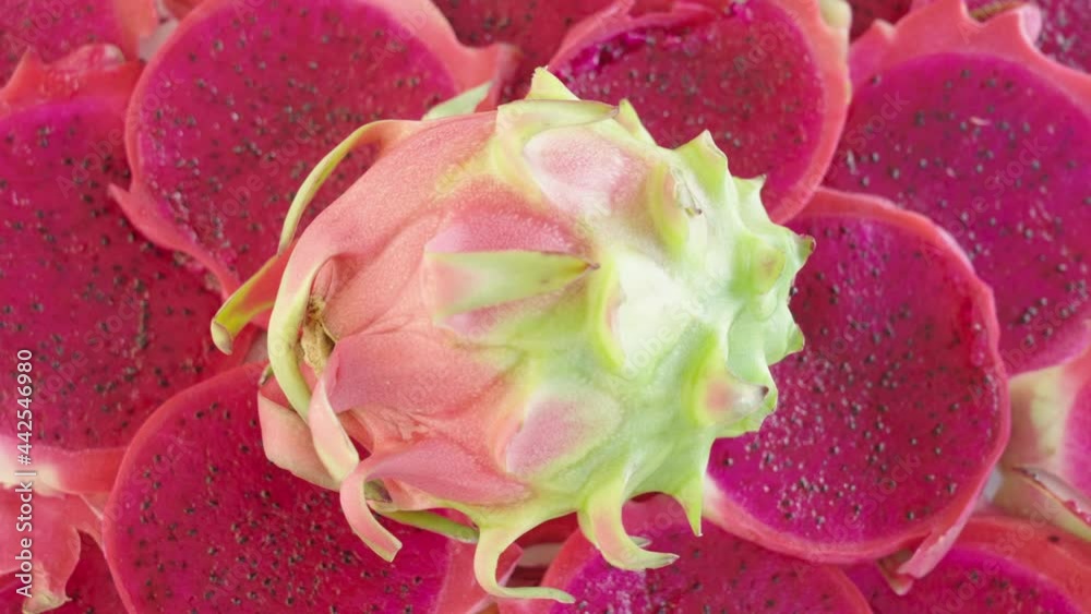 Pink and green whole dragon fruit on top of a texture of layered dragon ...