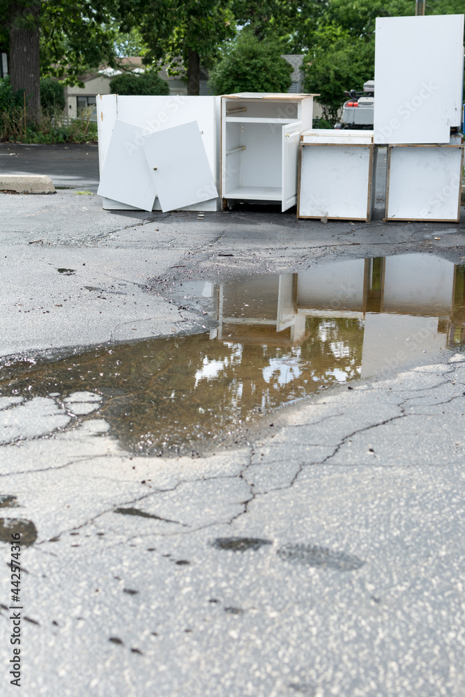 Old cabinets set out by dumpsters on trash day; reflection in puddle on ...