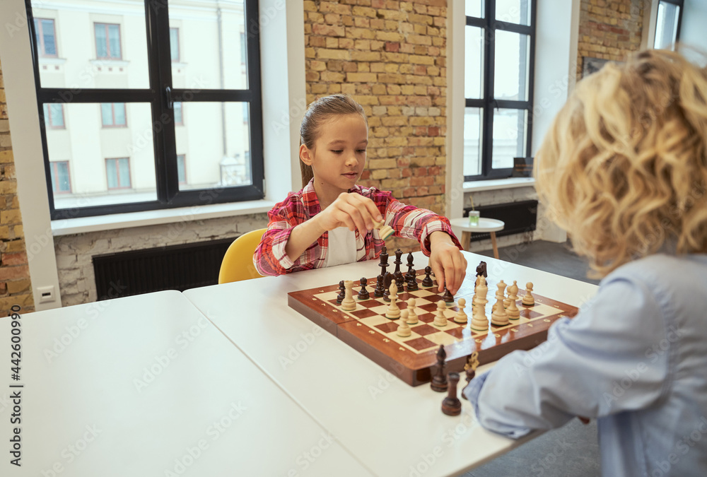 Worthy opponent. Beautiful little girl playing chess with her friend ...