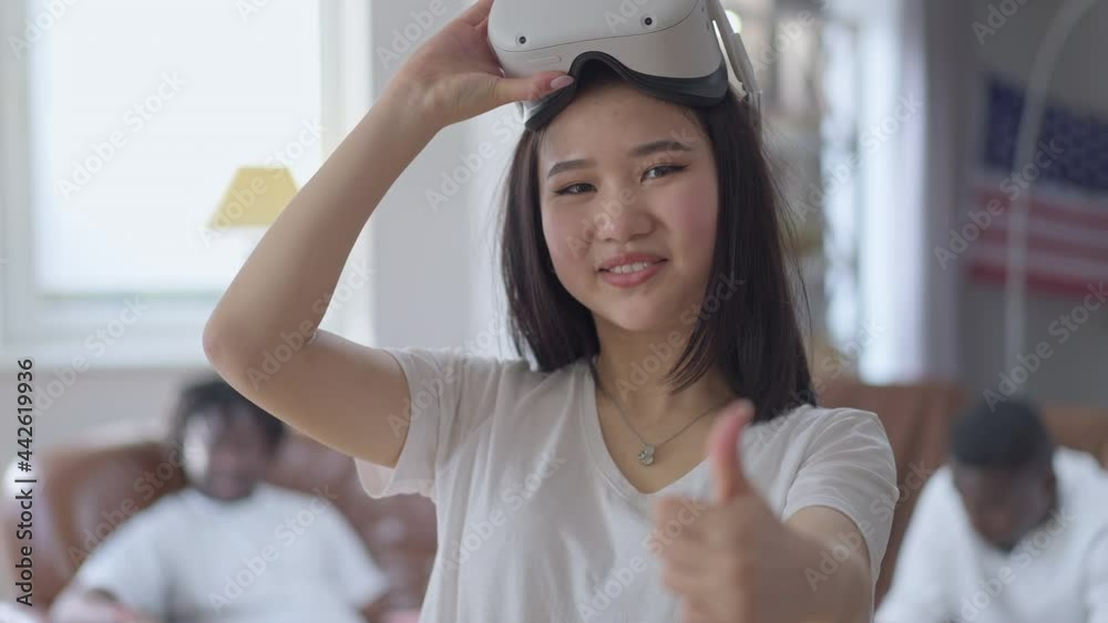 Positive Asian woman taking off VR headset showing thumb up looking at ...