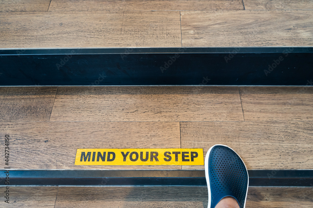 Yellow and black warning sign on wooden stairs is mind your step .Put ...