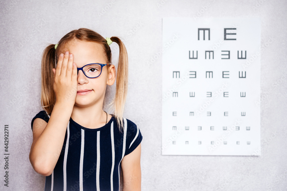 Little girl wearing eyeglasses taking eyesight test before school with ...