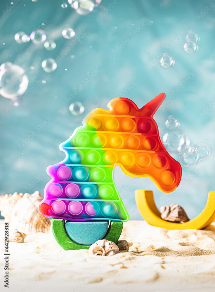 Pop it toy, rainbow colors, in the form of a unicorn on the podium on a ...