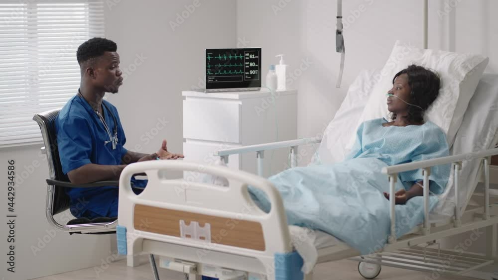 An African male doctor interviews a patient lying in a hospital bed ...