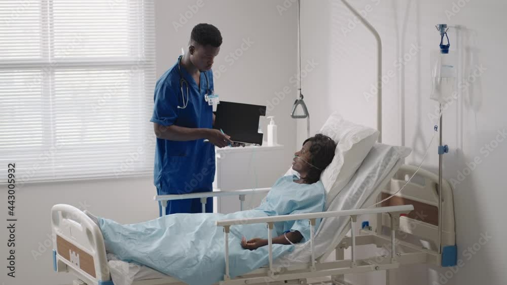 A black male doctor is talking to a black female patient lying on a ...