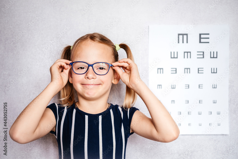 Happy little girl wearing eyeglasses taking eyesight test before school ...