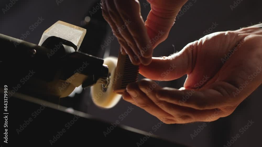 close-up. wood craftsman polishes a handmade wooden beard comb on a ...