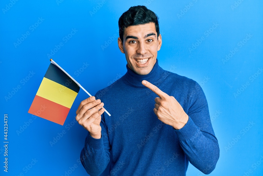 Handsome hispanic man holding belgium flag smiling happy pointing with ...