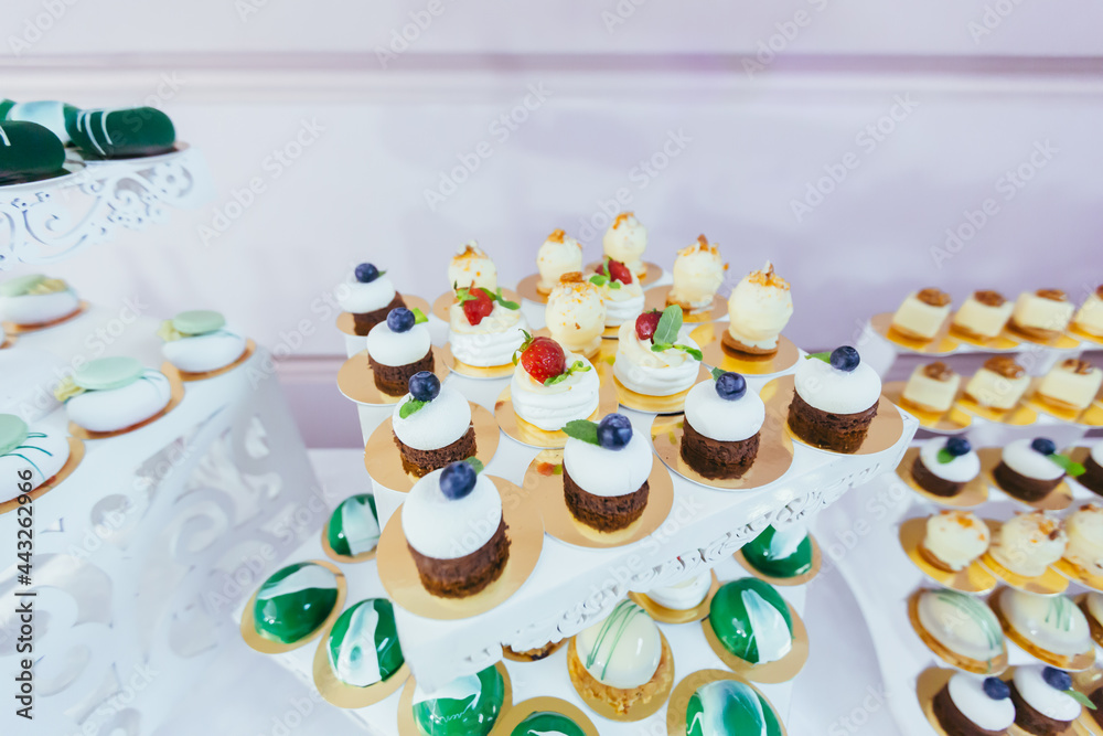 Candy bar. White festive table with deserts, strawberry tartlet and ...