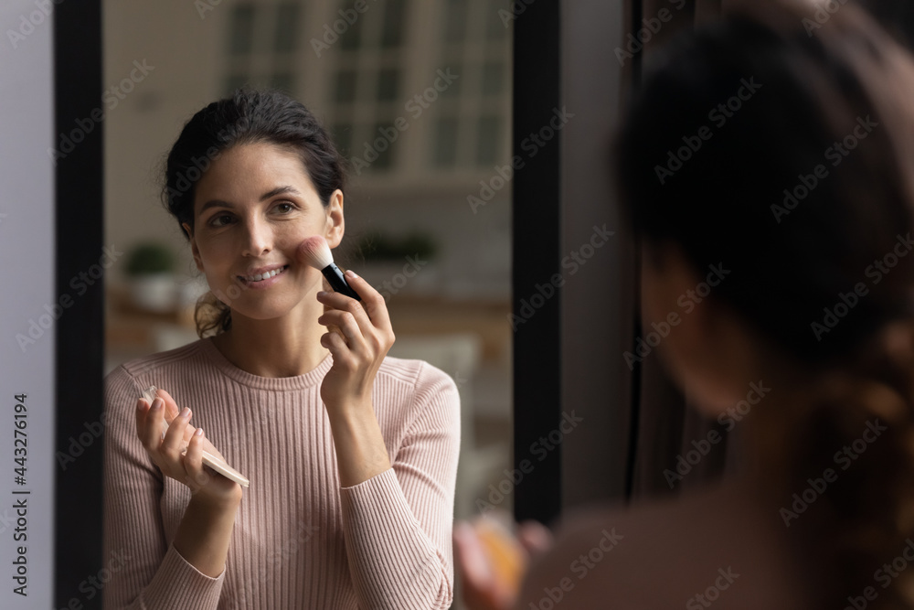 Mirror reflection attractive young woman applying powder rosy blushes ...