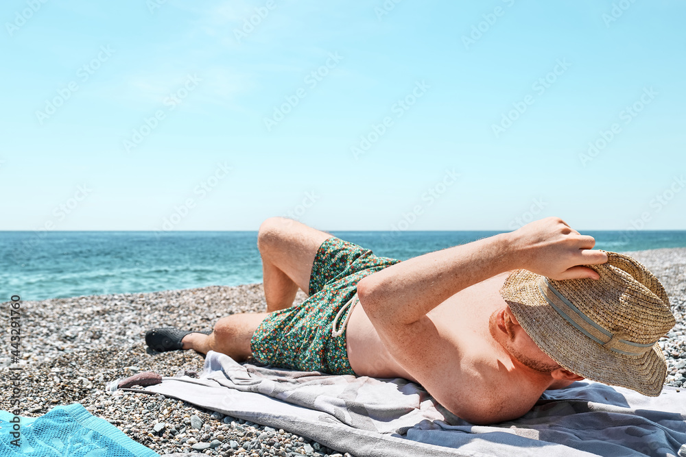 Young handsome red-haired man lying down on the beach shirtless wearing ...