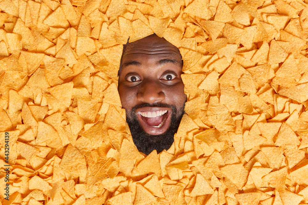 Positive dark skinned bearded Afro American man buried in chips looks ...