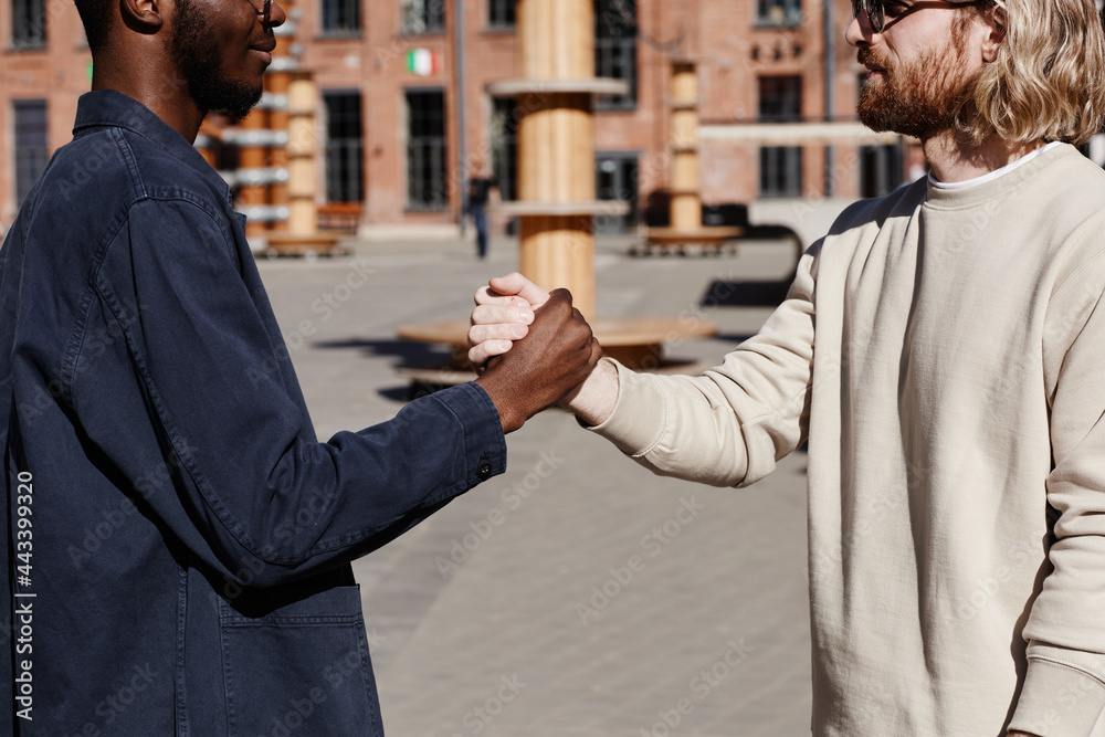 Side view portrait of two men greeting each other outdoors in city with ...