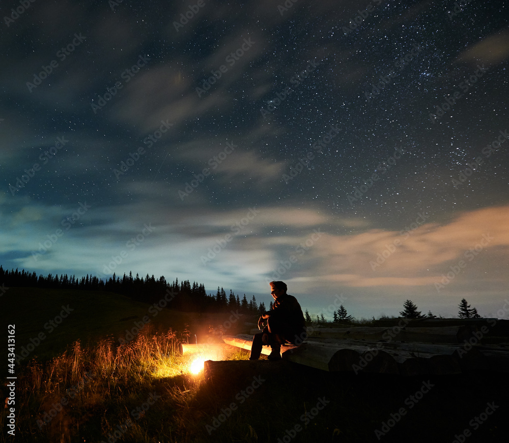 Young man tourist sitting on logs near campfire in the mountains under ...
