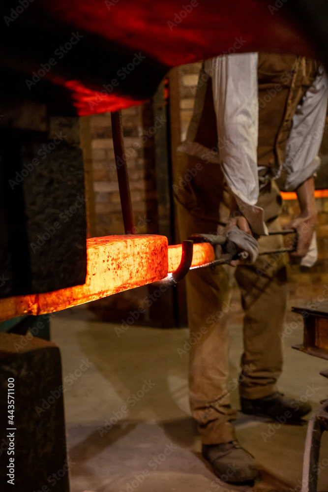 Foundry worker old blacksmith in protective clothing forming steel from ...