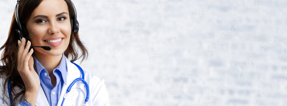 Portrait of happy smiling female doctor in headset, over white brick ...