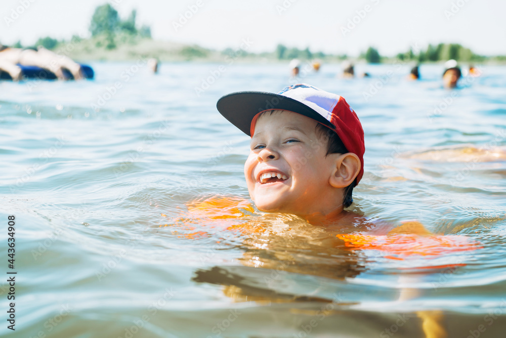 Portrait of a laughing little boy swimming in the water, outdoors ...