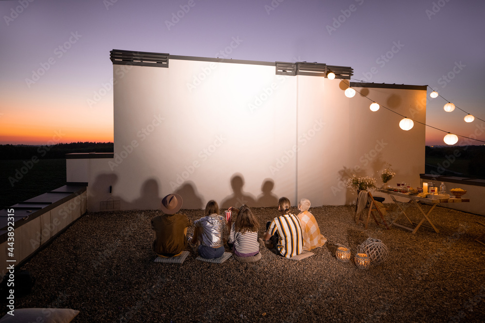 Small group of people watching movie on the rooftop terrace at sunset ...