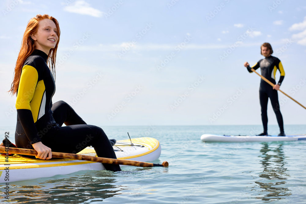 Happy positive couple paddling on SUP board at sea at sunny day. Stand ...