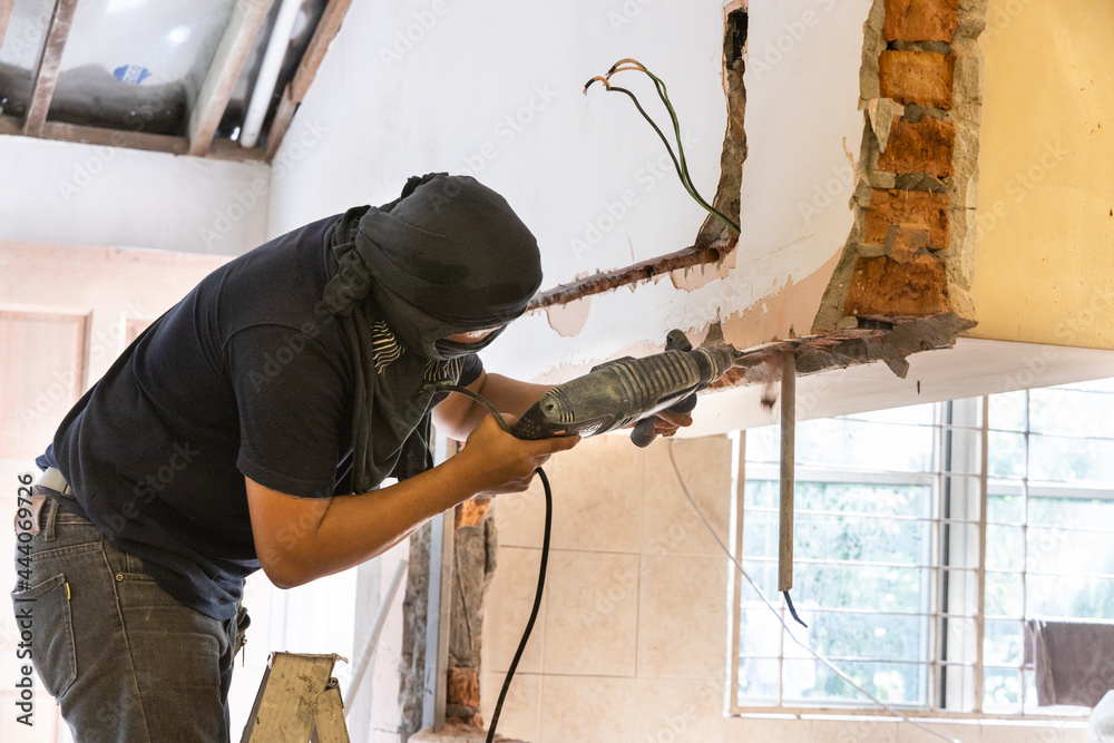 Worker drilling on wall to create cavity for electric power cables in ...