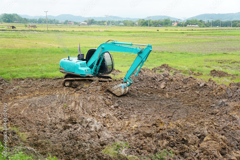 A blue excavator is digging a swamp in the middle of a field for ...