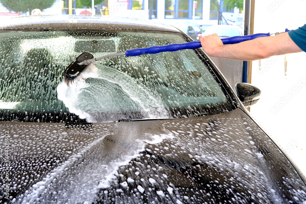 man washes his black car with water and foam at a self-service car wash ...