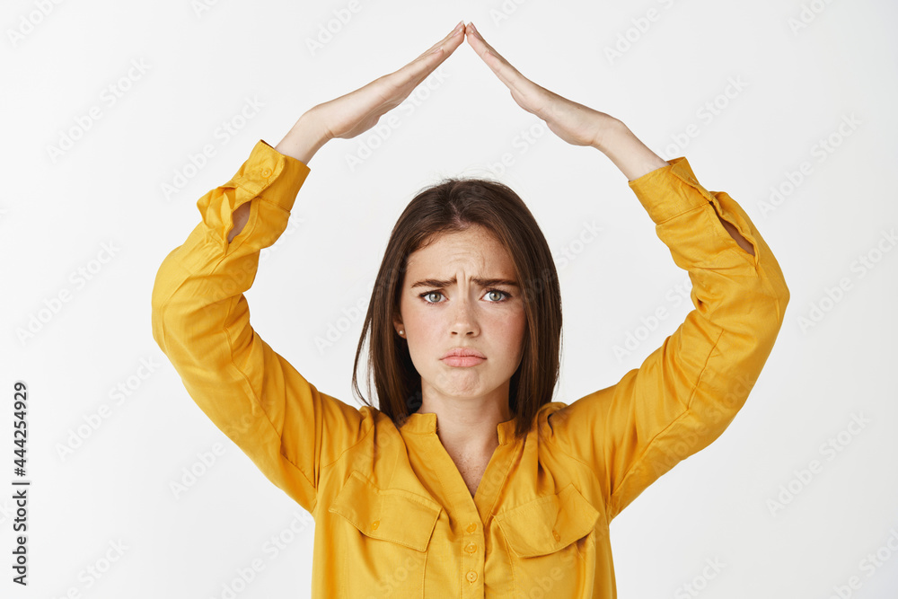 Sad young woman frowning and pouting, showing home roof with hands ...
