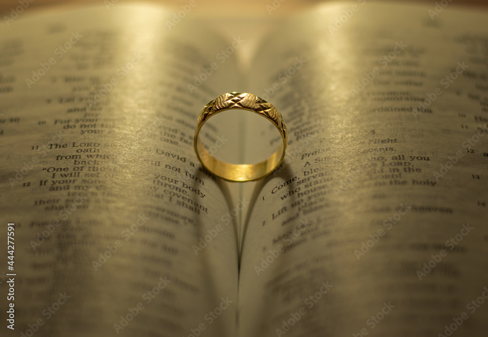 Shiny golden engagement ring on open Holy Bible shadow forming heart ...