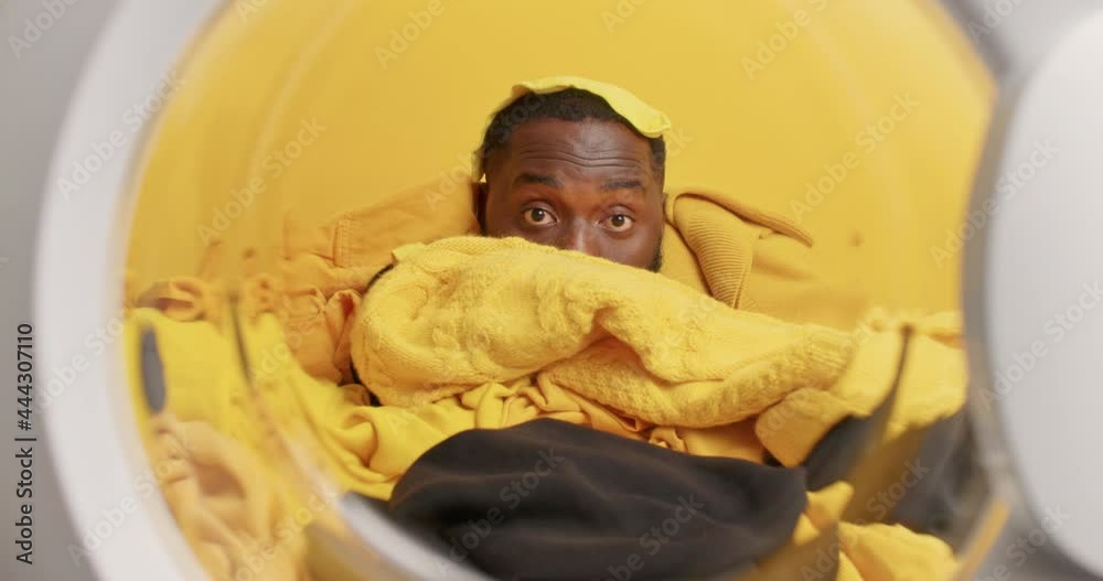 Shocked embarrassed dark skinned man buried in unfolded laundry poses ...