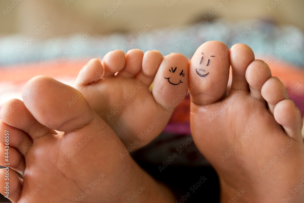 Close-up of bare feet sticking out from covers while couple lays in bed ...