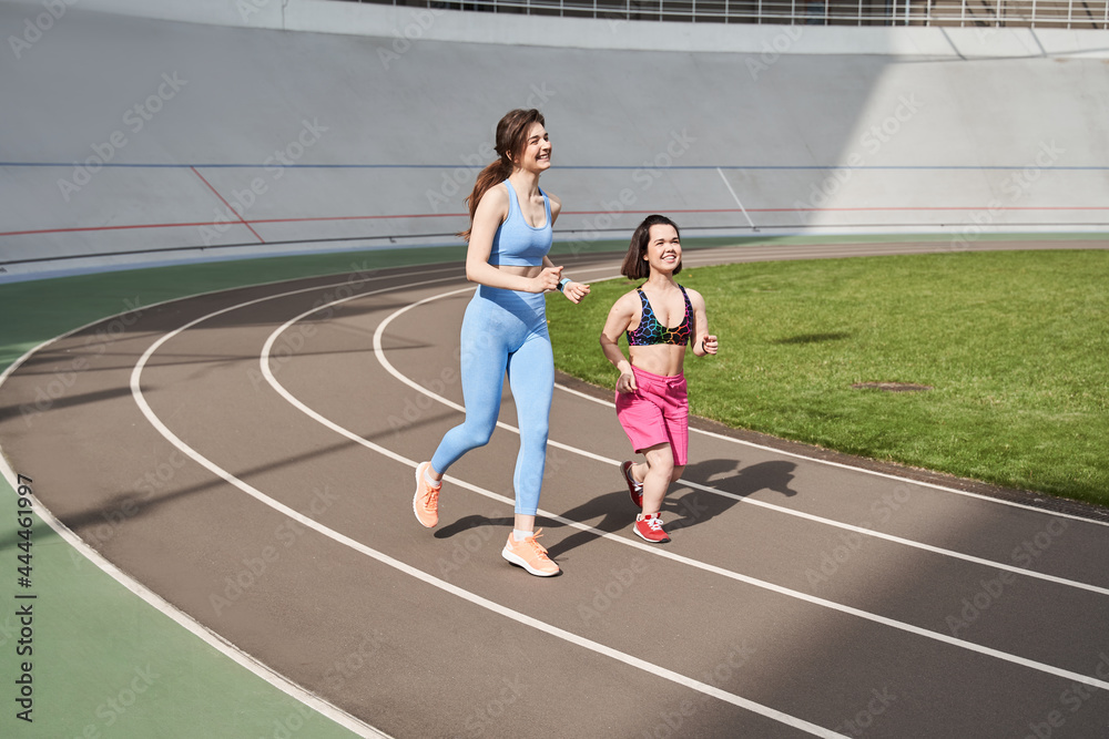 Girls jogging on running track in city stadium at the sunny morning ...