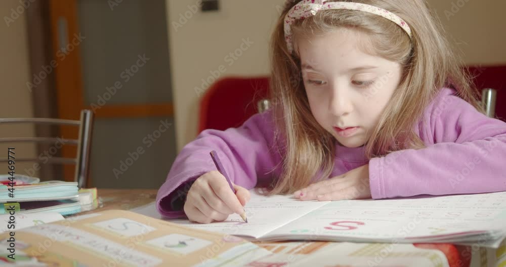 Little girl at home doing homework drawing on school's book with brown ...