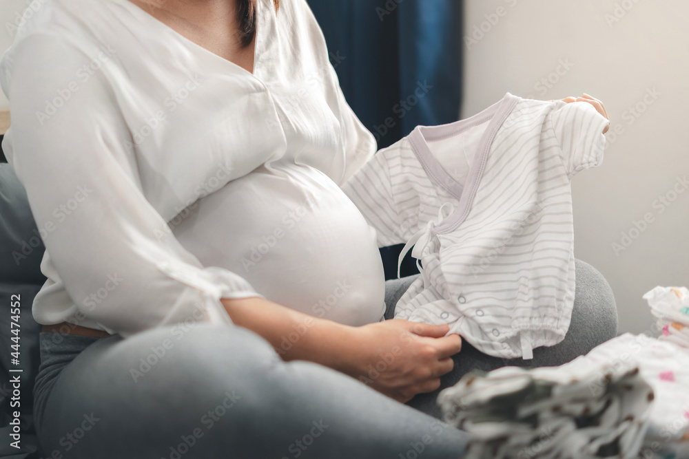 Pregnant asian woman prepare fold baby clothes for planning new born ...