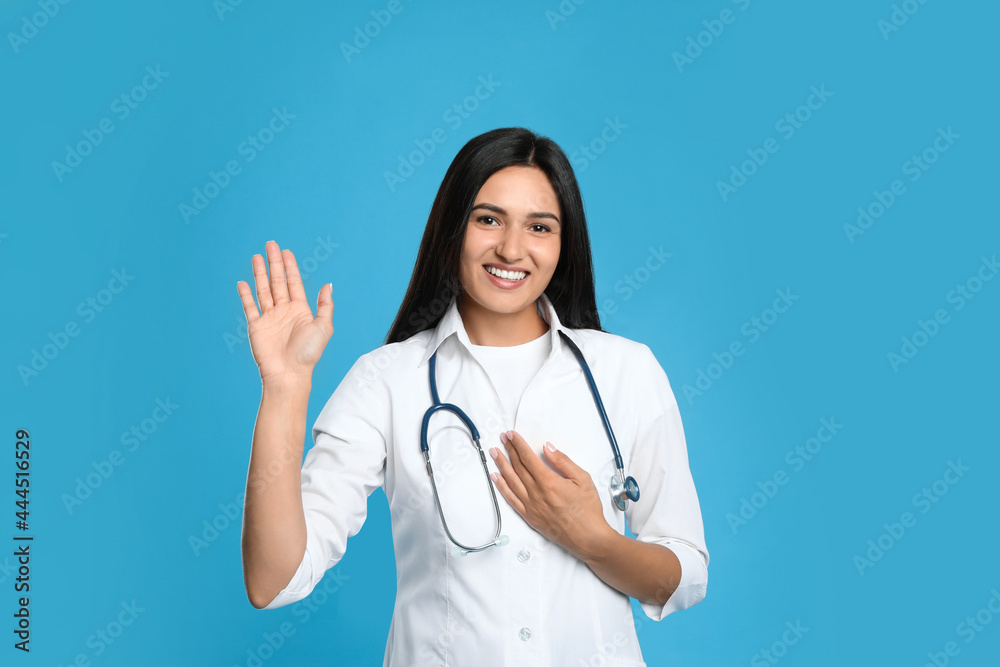 Happy female doctor waving to say hello on light blue background Stock ...