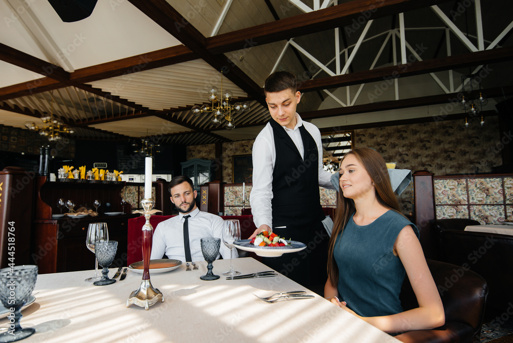 A stylish waiter serves a young couple who came on a date in a gourmet ...