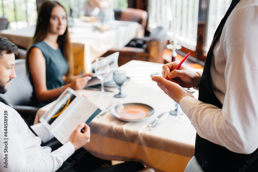 A stylish waiter serves a young couple who came on a date in a gourmet ...