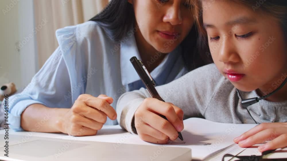 4K Asian young little girl using laptop to study with her mother. Student kid writing homework ...
