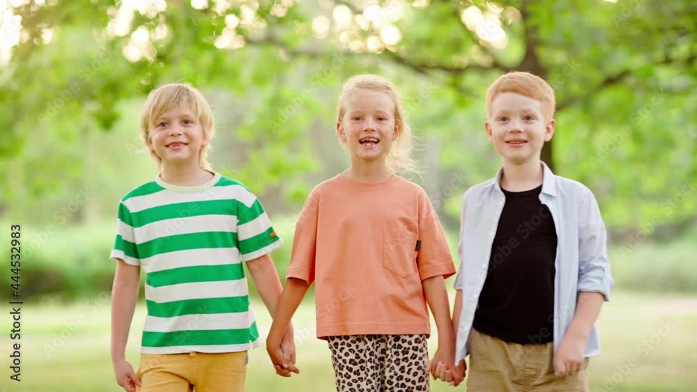 Zoom in of three cute kids, two boys and girl, standing holding hands ...