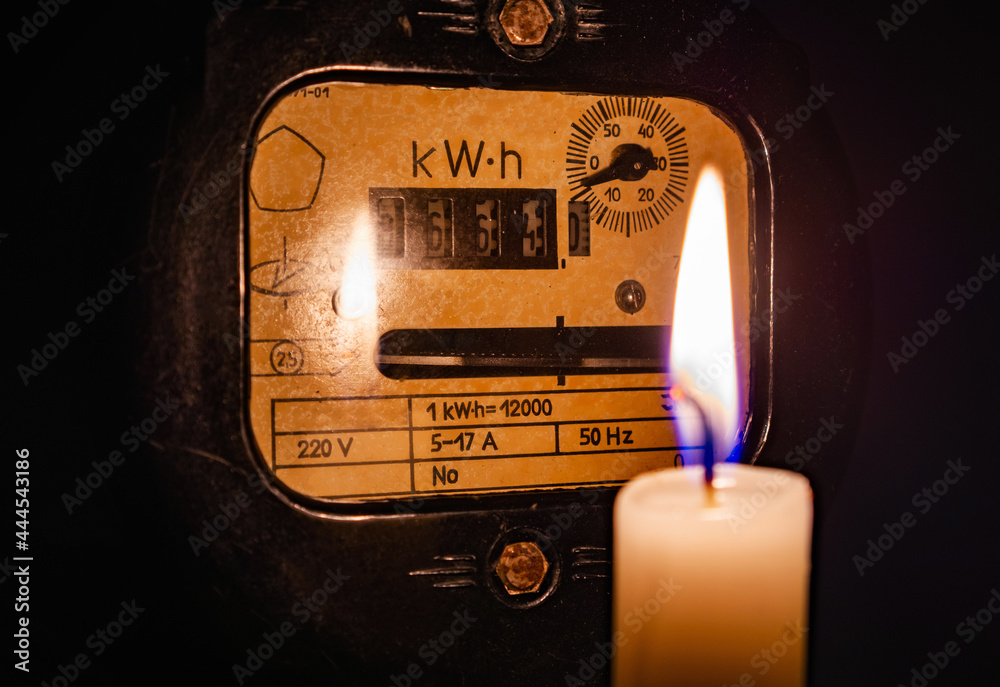 Old domestic electricity meter illuminated by the light of a burning ...