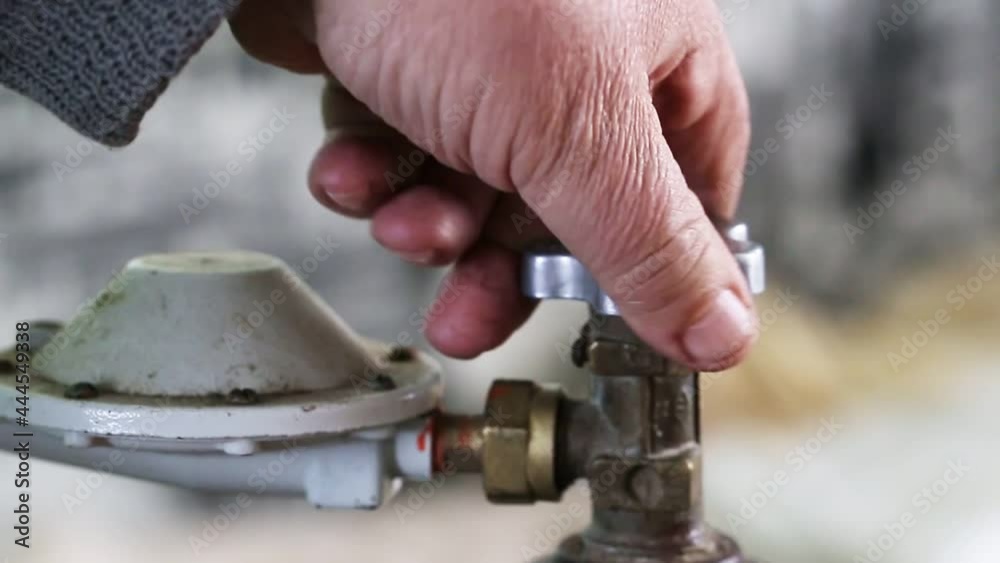 A man closes the valve of a gas cylinder with his hand, close-up ...