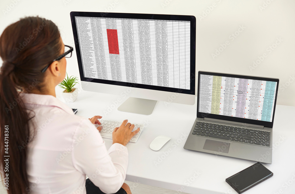 Young woman sitting at white office desk, looking at screens of desktop ...