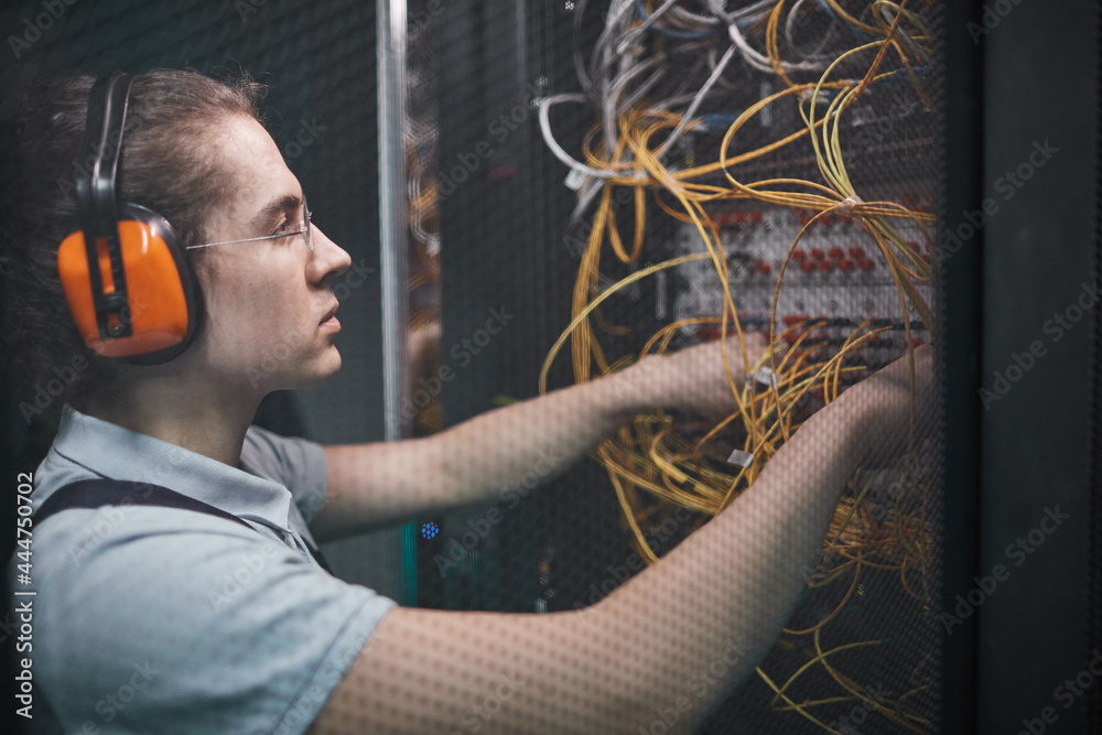 Side view of young network engineer connecting cables in server room ...