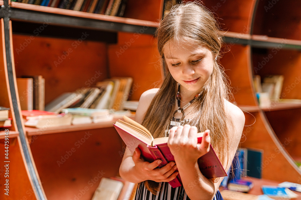 Cute little girl in the library in the park holding books. Togliatti ...