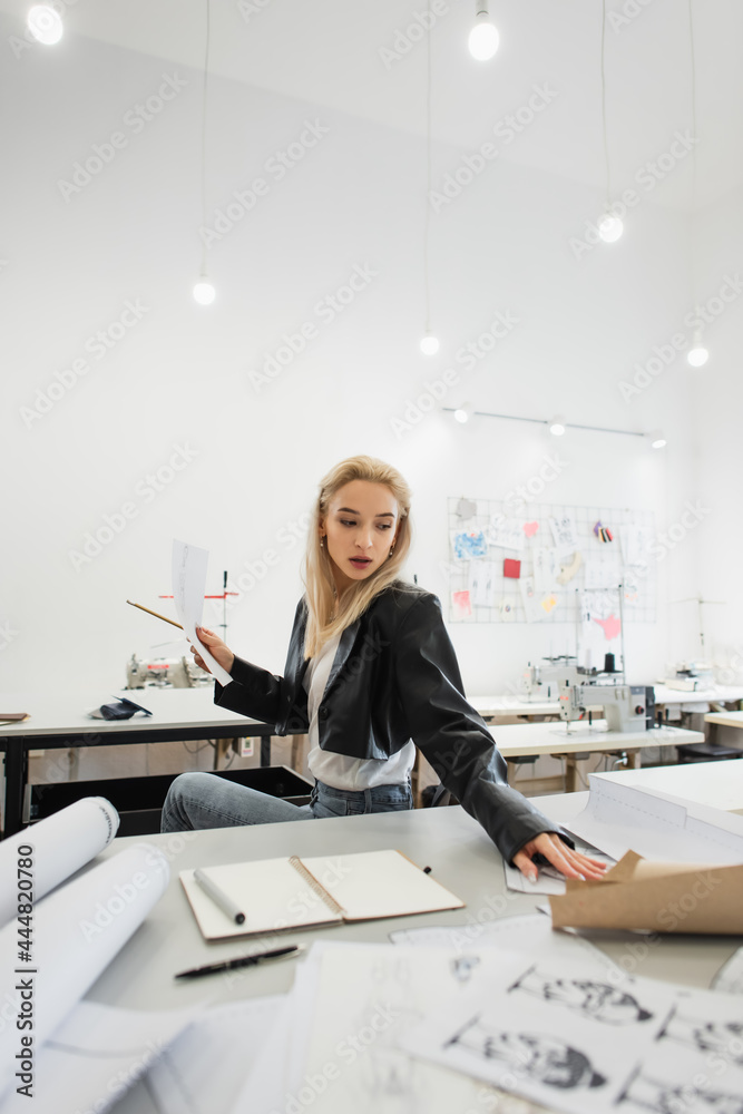 fashion designer holding paper and pencil while looking at sewing ...