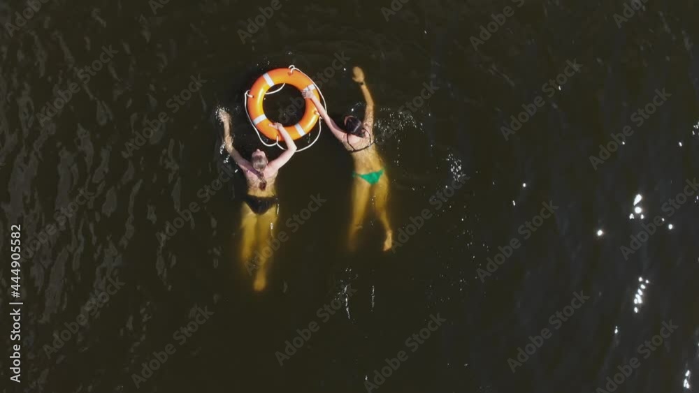 Two young caucasian women swim in the dark muddy water using life buoy ...