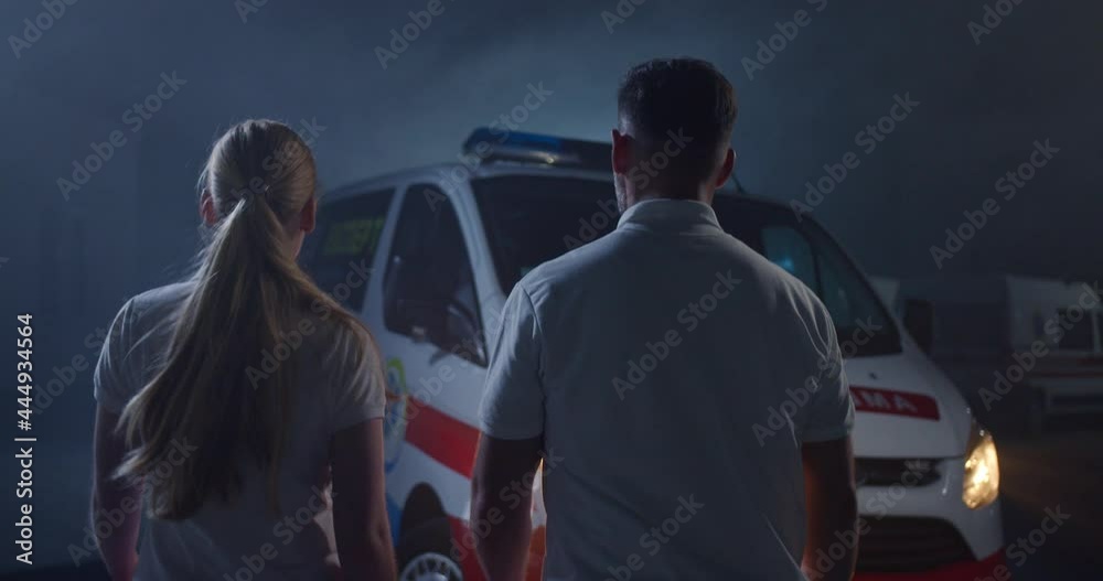 Rear on couple of paramedics walking fast to ambulance car at night ...