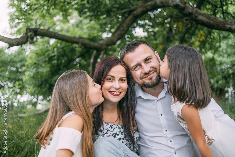 Two pretty sisters kissing their father and mother during summer picnic ...