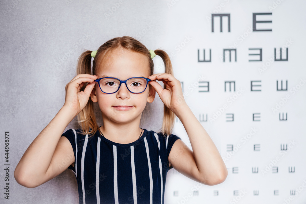 Happy little girl wearing glasses taking eyesight test before school ...