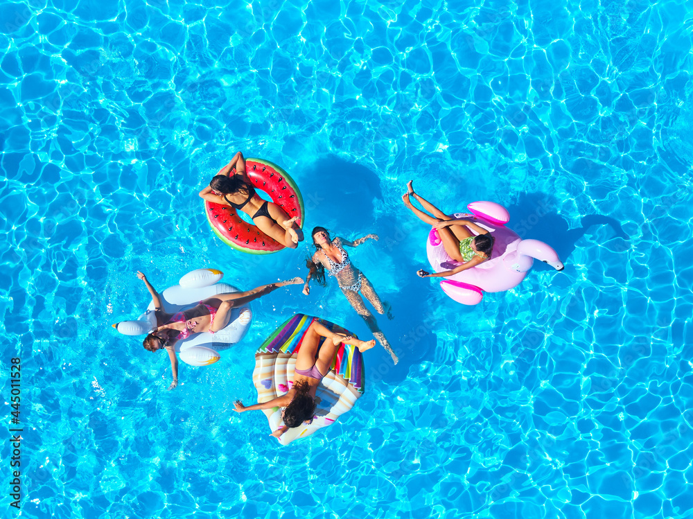 Aerial of hot pretty girls in bikini swimming in pool on floaties. Top ...