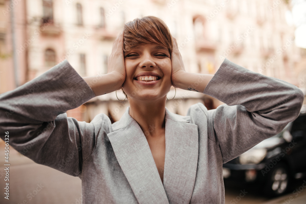 Lady in grey suit smiling and covering her ears. Short-haired good ...